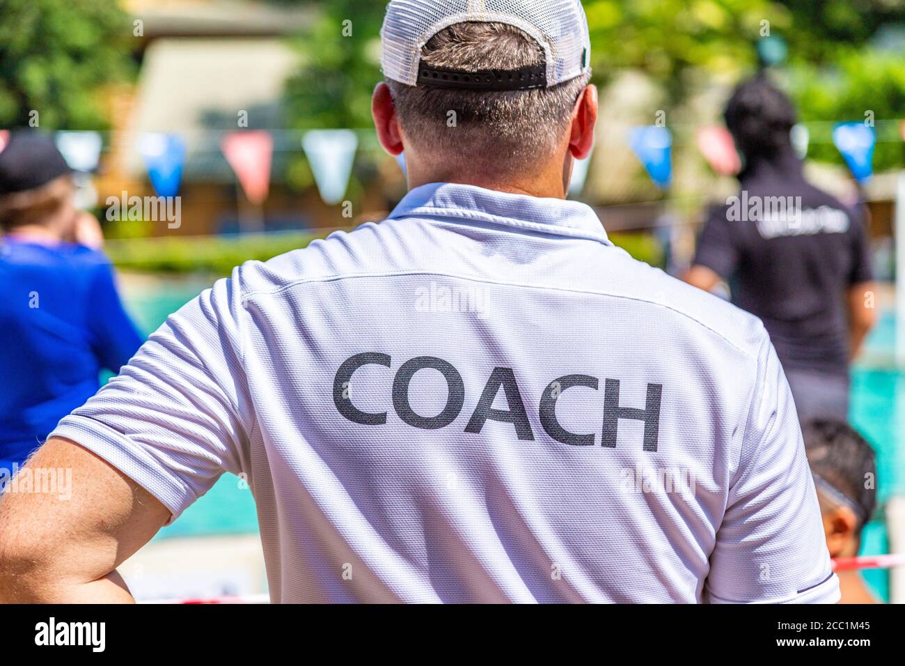 Male swimming coach in white COACH shirt standing in the sun watching ...