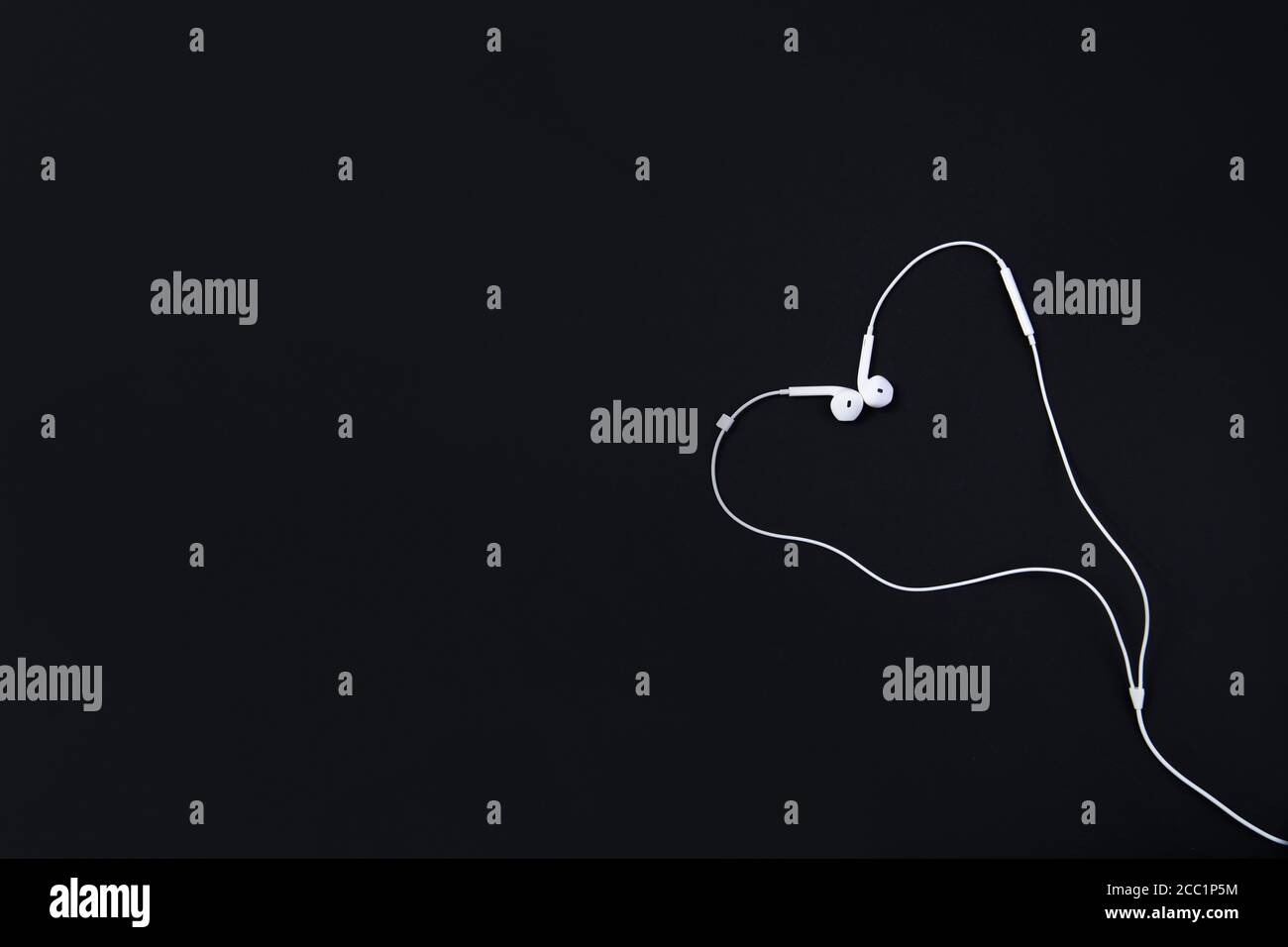 white headphones lie on a black background in the shape of a heart ...