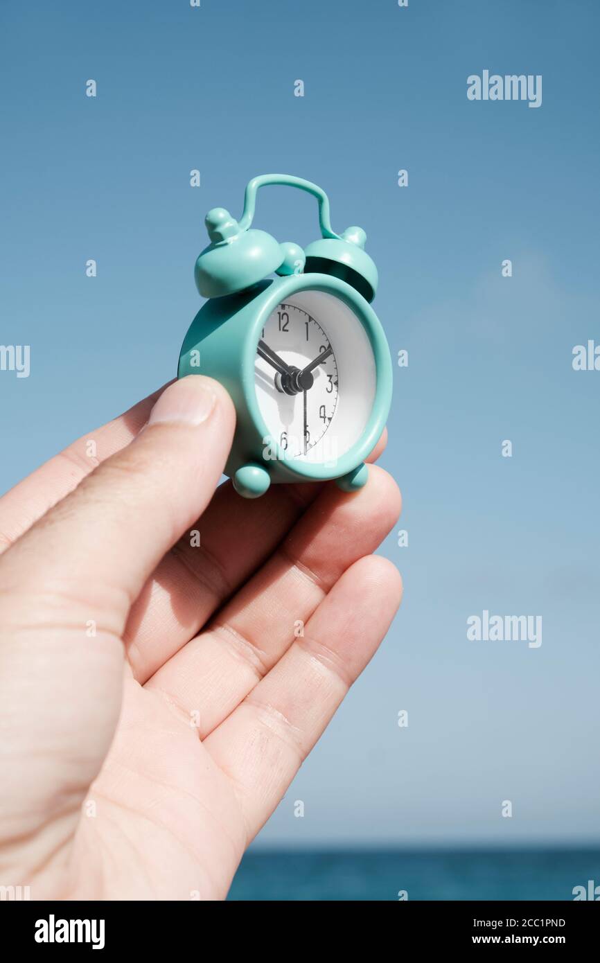 closeup of a caucasian man holding a small pastel green alarm clock in ...