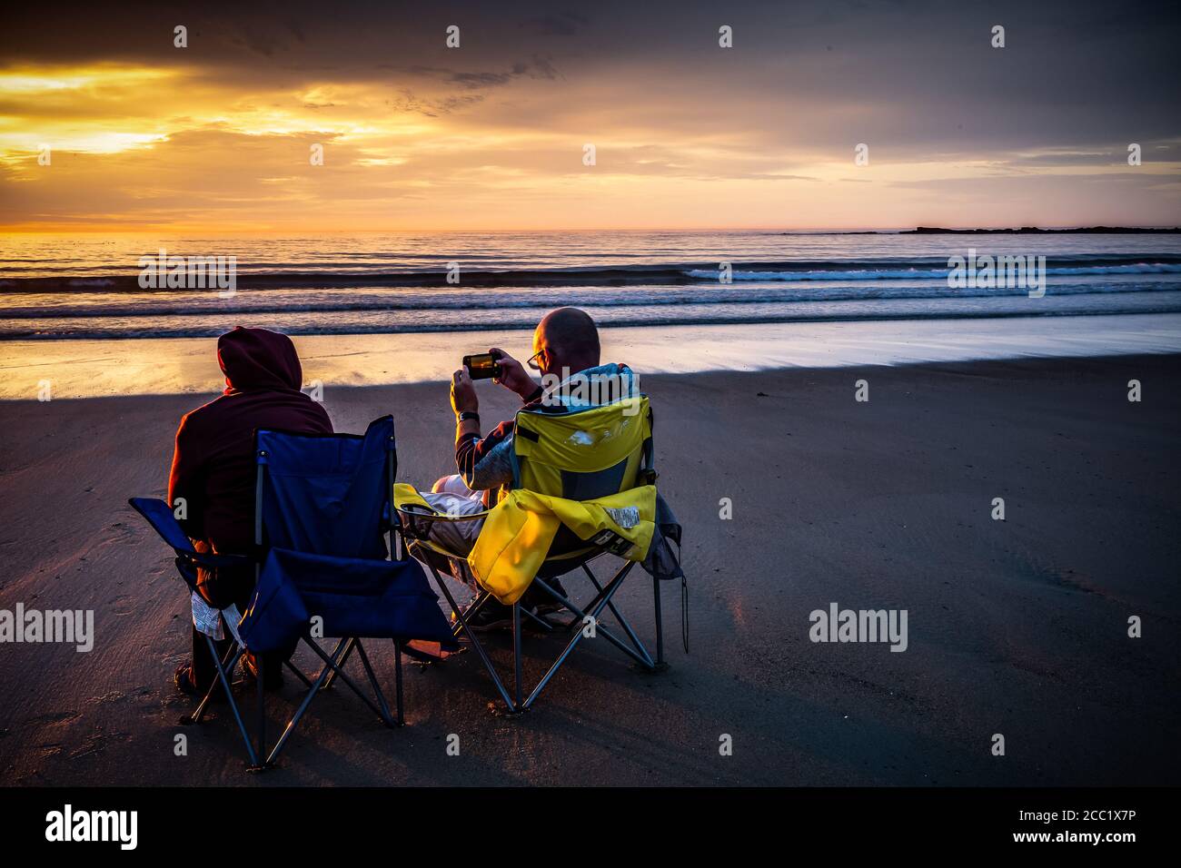 A couple sitting on the beach watching taking photographs with their ...