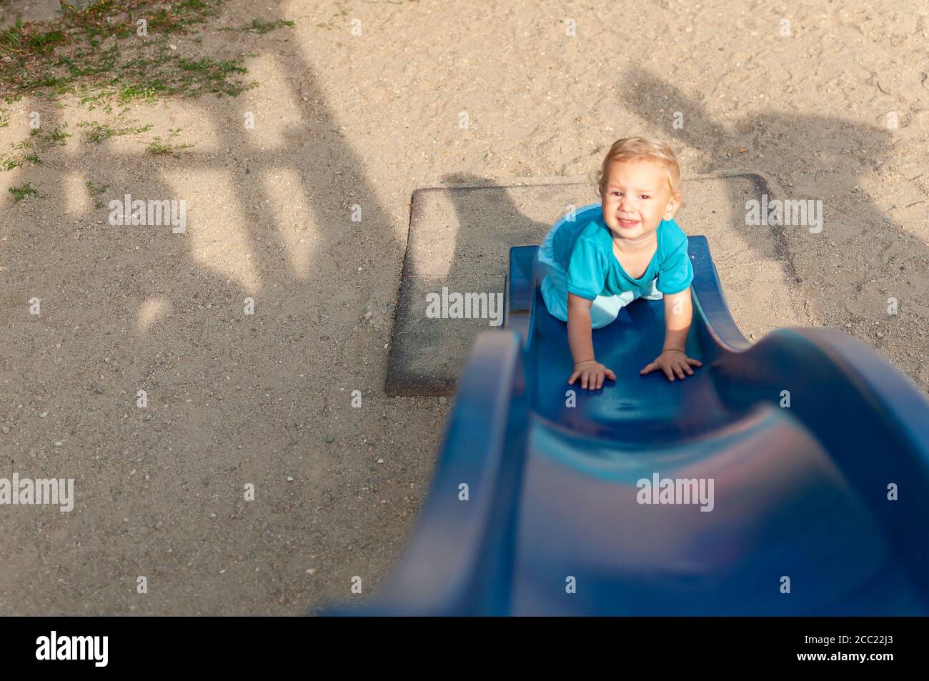 Child playing and climbing a blue slide at a playground Stock Photo - Alamy