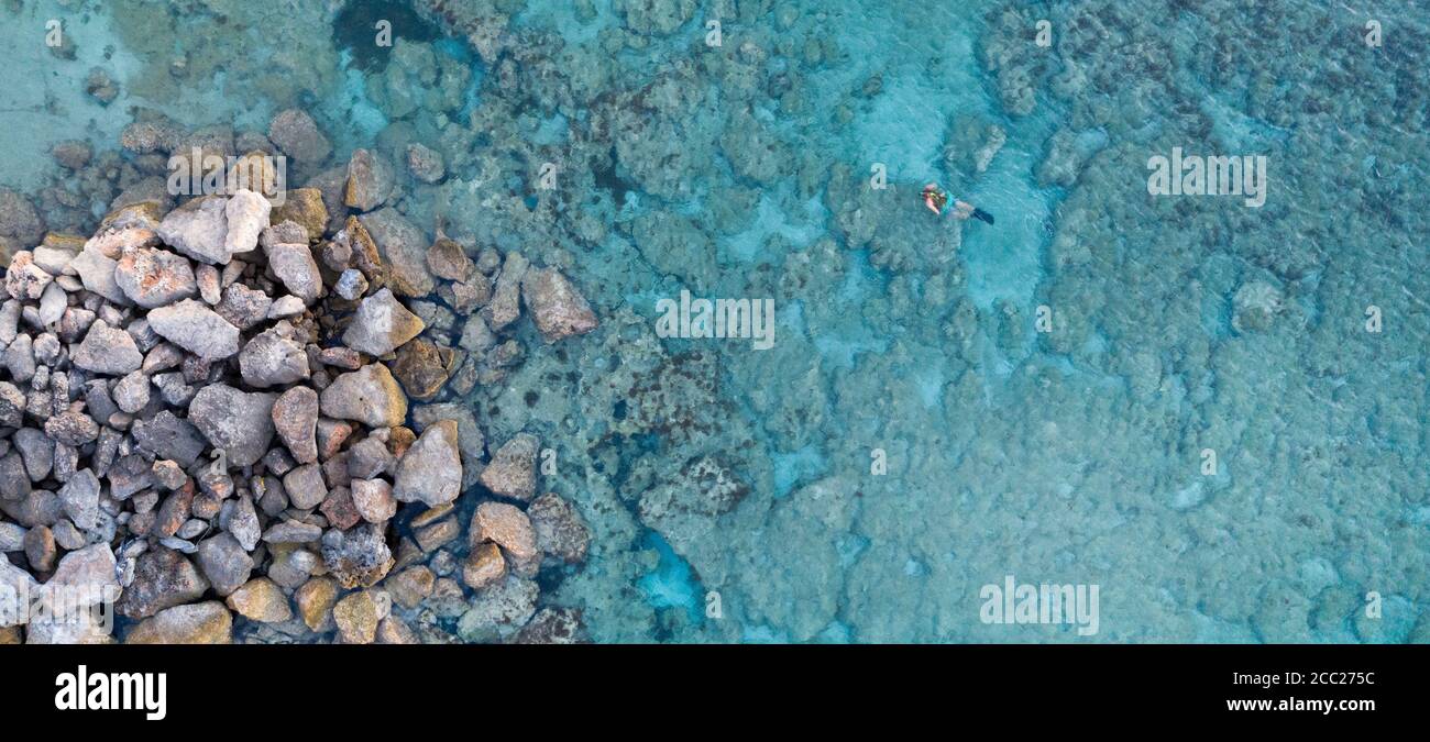 Aerial shot of a person swimming in the sea surrounded by rocks in ...
