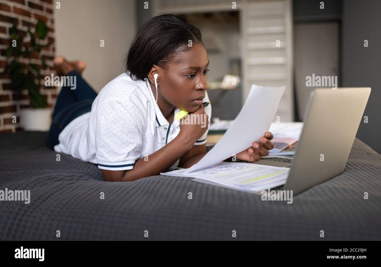 Pensive ethnic student reading data from document during remote lesson ...