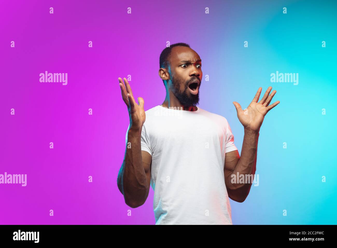 Shocked, astonished. African-american young man's portrait on gradient studio background in neon ...
