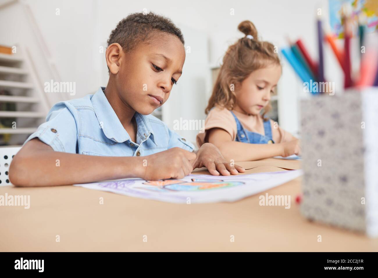 Portrait of cute African-American boy coloring pictures with crayons ...