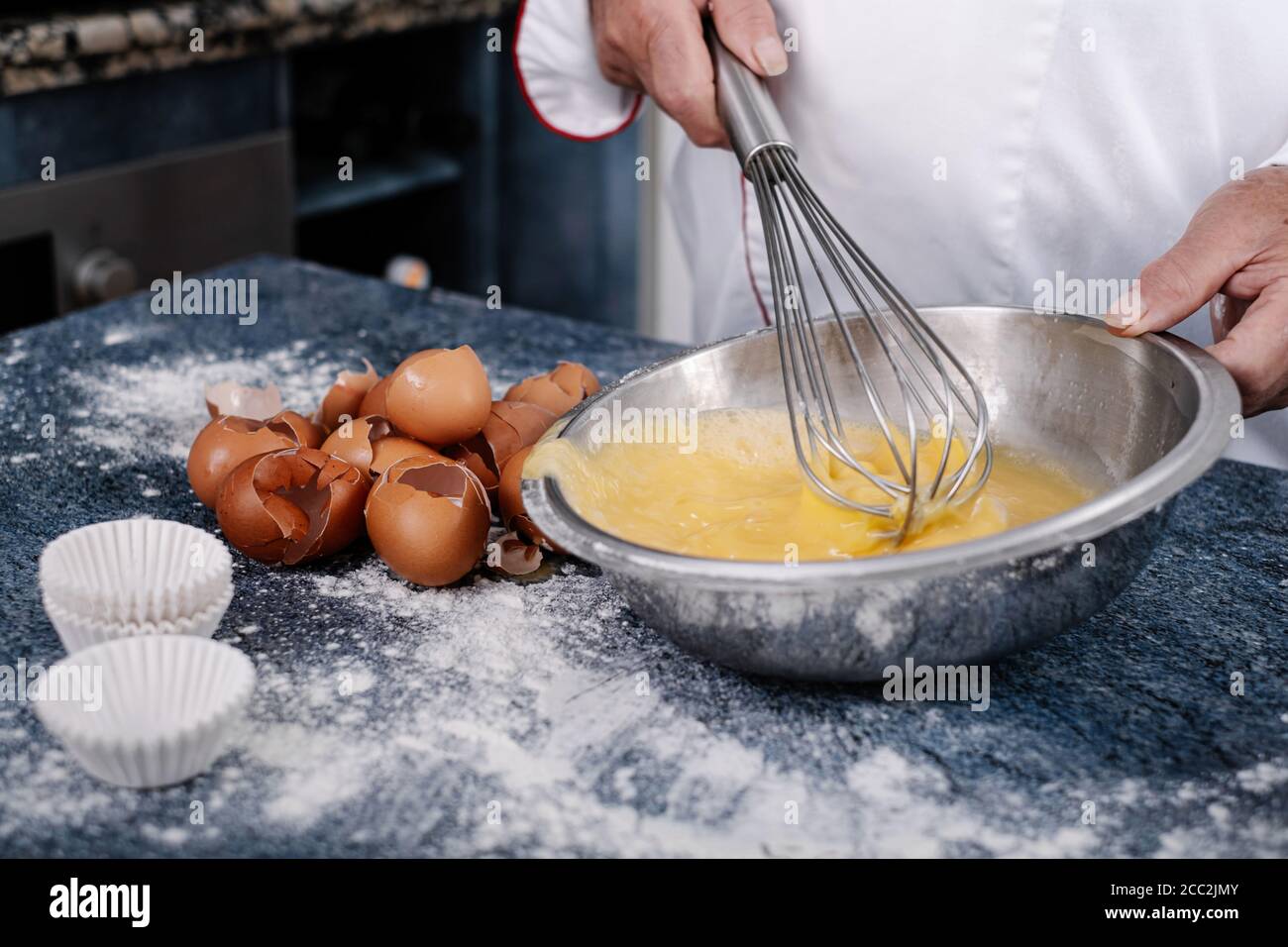 Close-up of a baker mixing eggs with a hand blender in a steel bowl ...