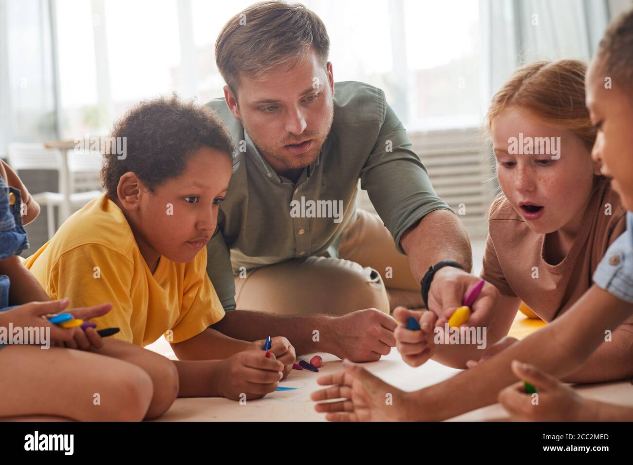 Portrait of young male teacher working with kids drawing pictures while ...