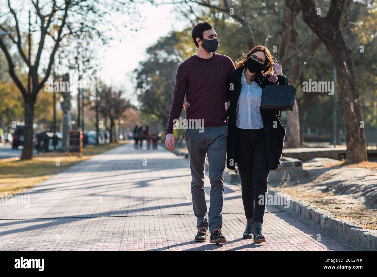Shot of a couple with masks walking in a park - the new normal concept ...