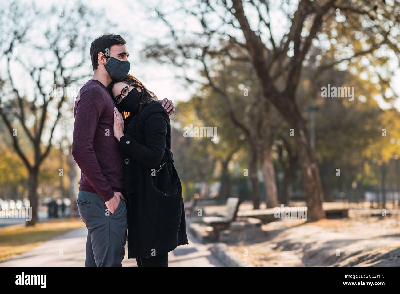 Shot of a couple with masks hugging each other in a park - the new ...