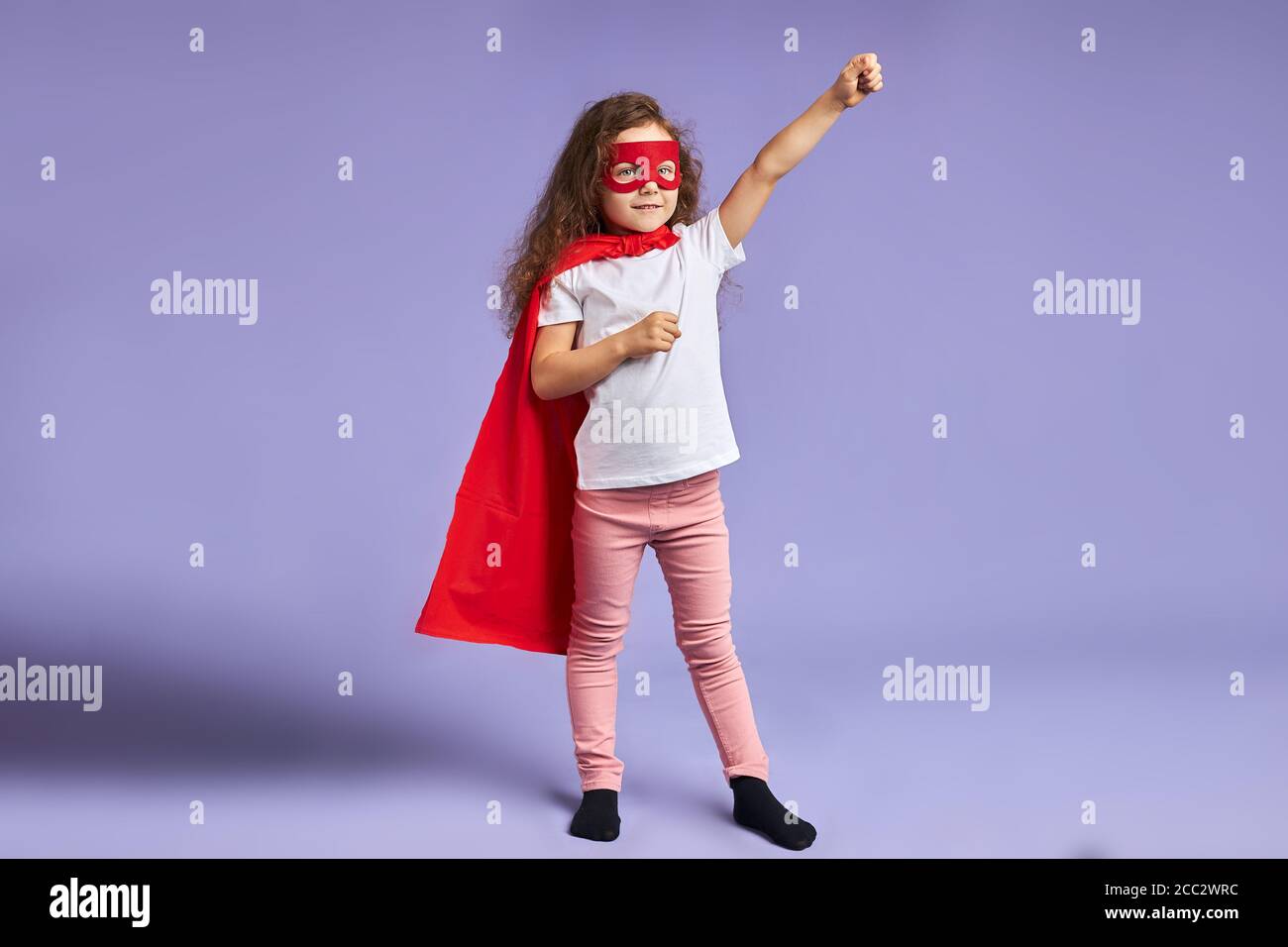 Spaceman concept. Little girl in red mask and cloak raised arms up ...