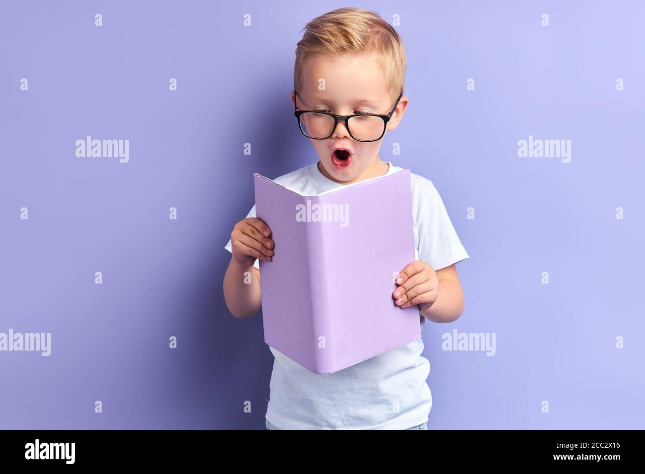 Sweet boy wearing white t-shirt and glasses for eyes reading book with ...
