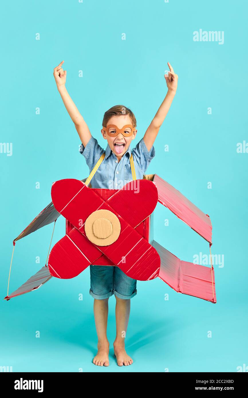 Happy smiling boy raised hands up at sky while flying on cardboard box ...