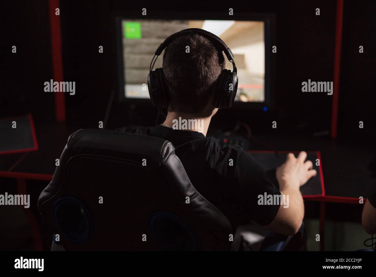 Rear view of focused young gamers sitting in line behind monitors in ...