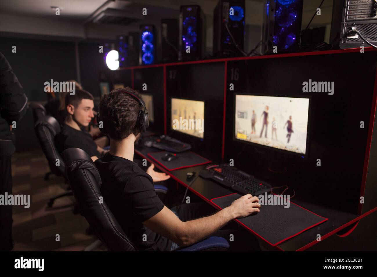 Rear view of focused young gamers sitting in line behind monitors in ...