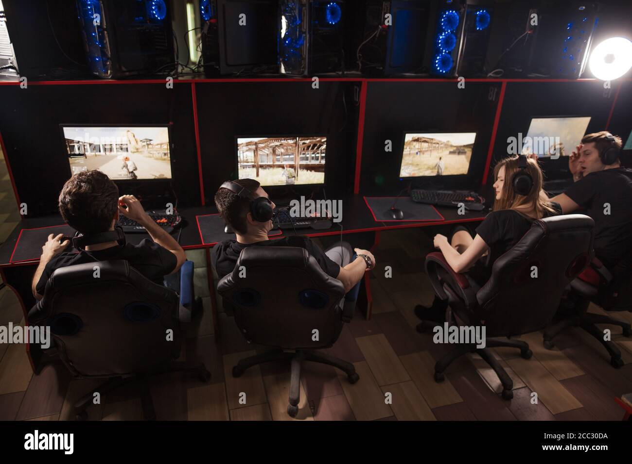 Rear view of focused young gamers sitting in line behind monitors in ...