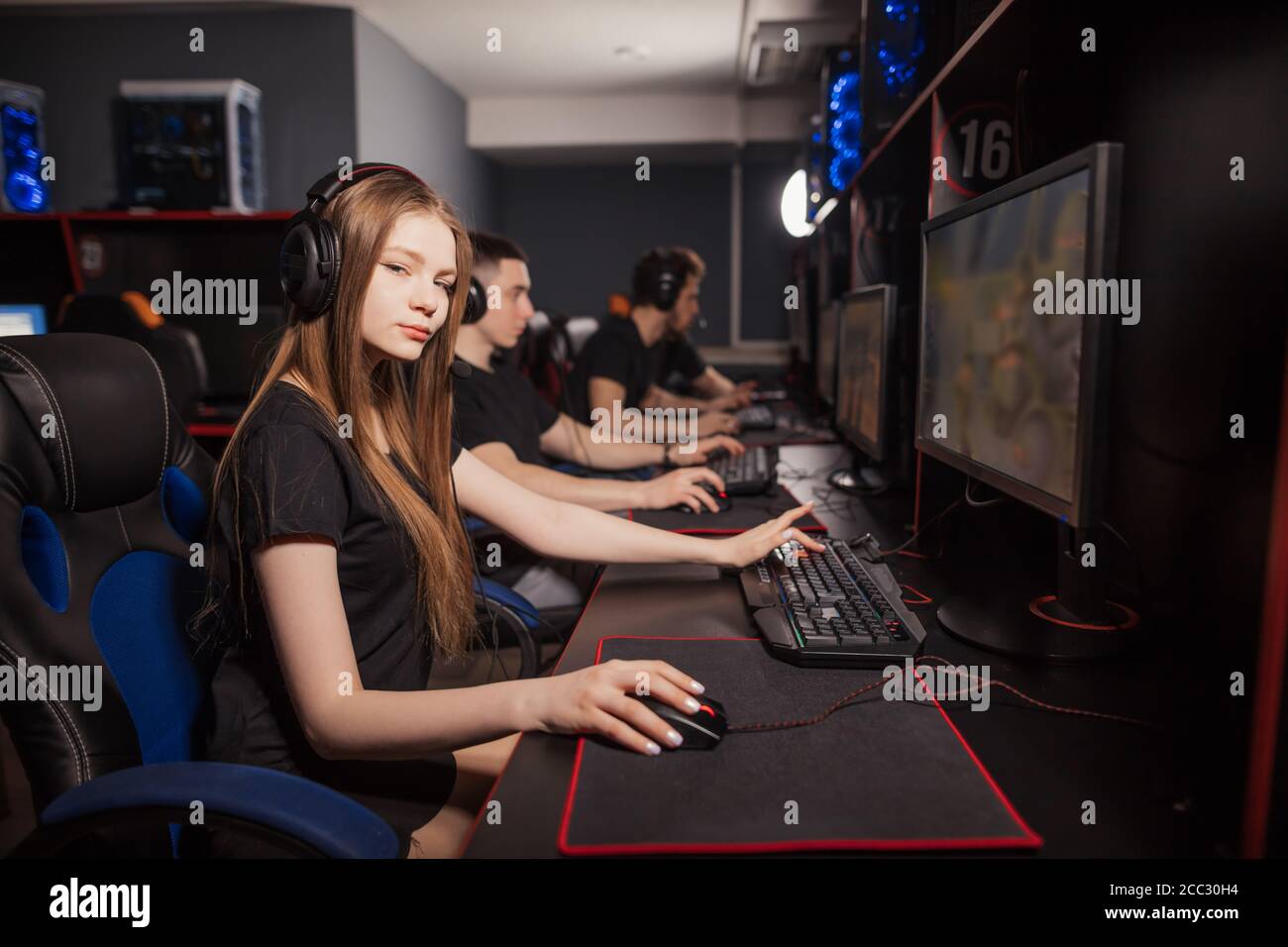 A cute female gamer girl with headset sits in a dark room behind a ...
