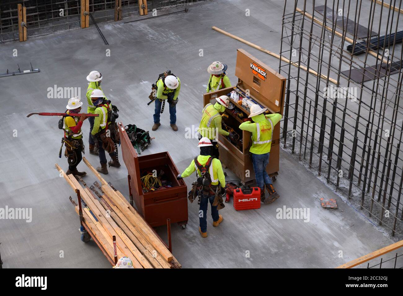 Construction workers wearing safety gear and face coverings gather ...