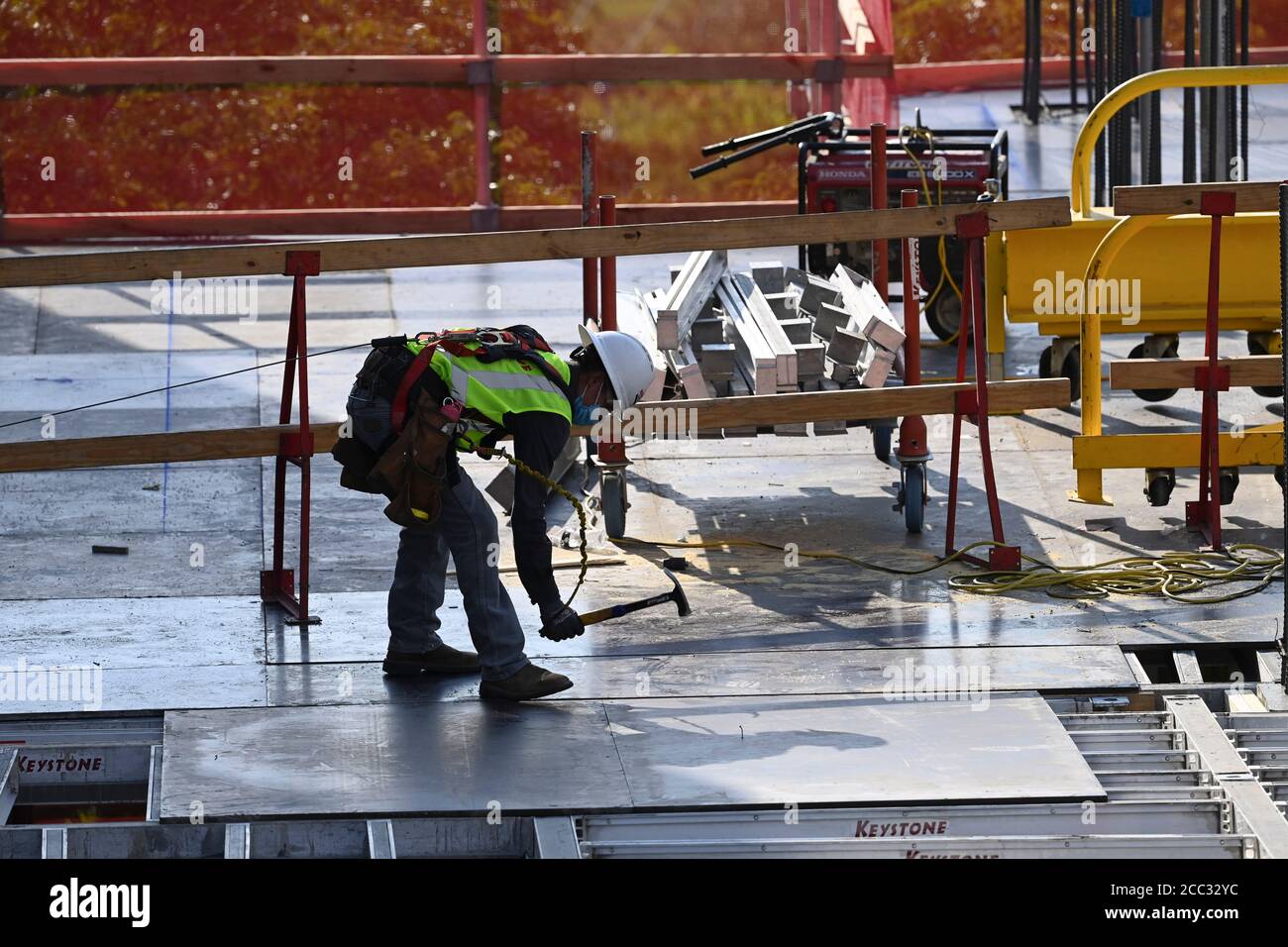 Construction worker wearing safety gear and face covering uses hammer ...