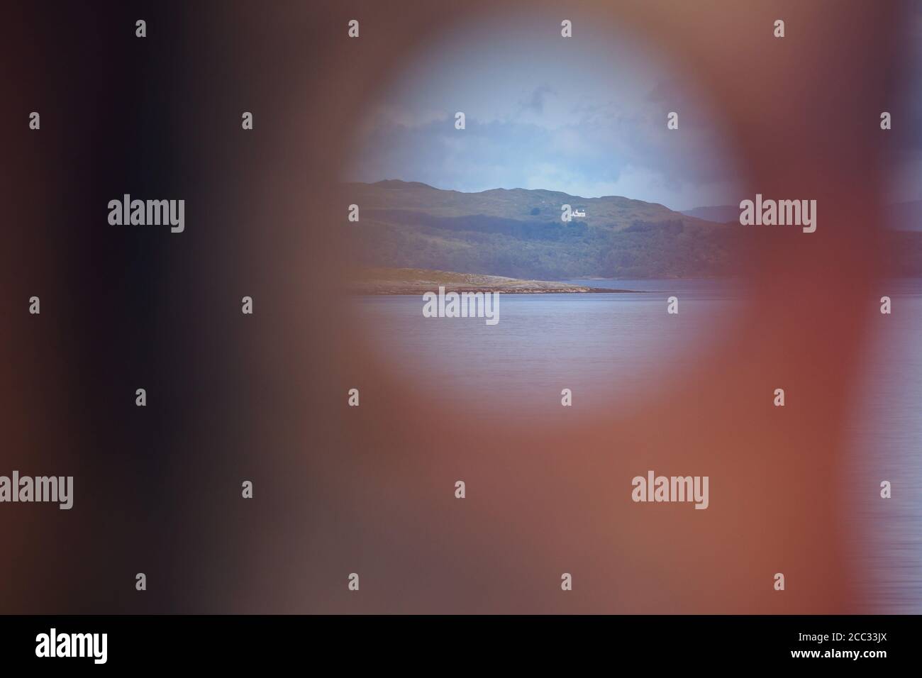 A view looking through a hole in a rusty post on a pier across the sea ...