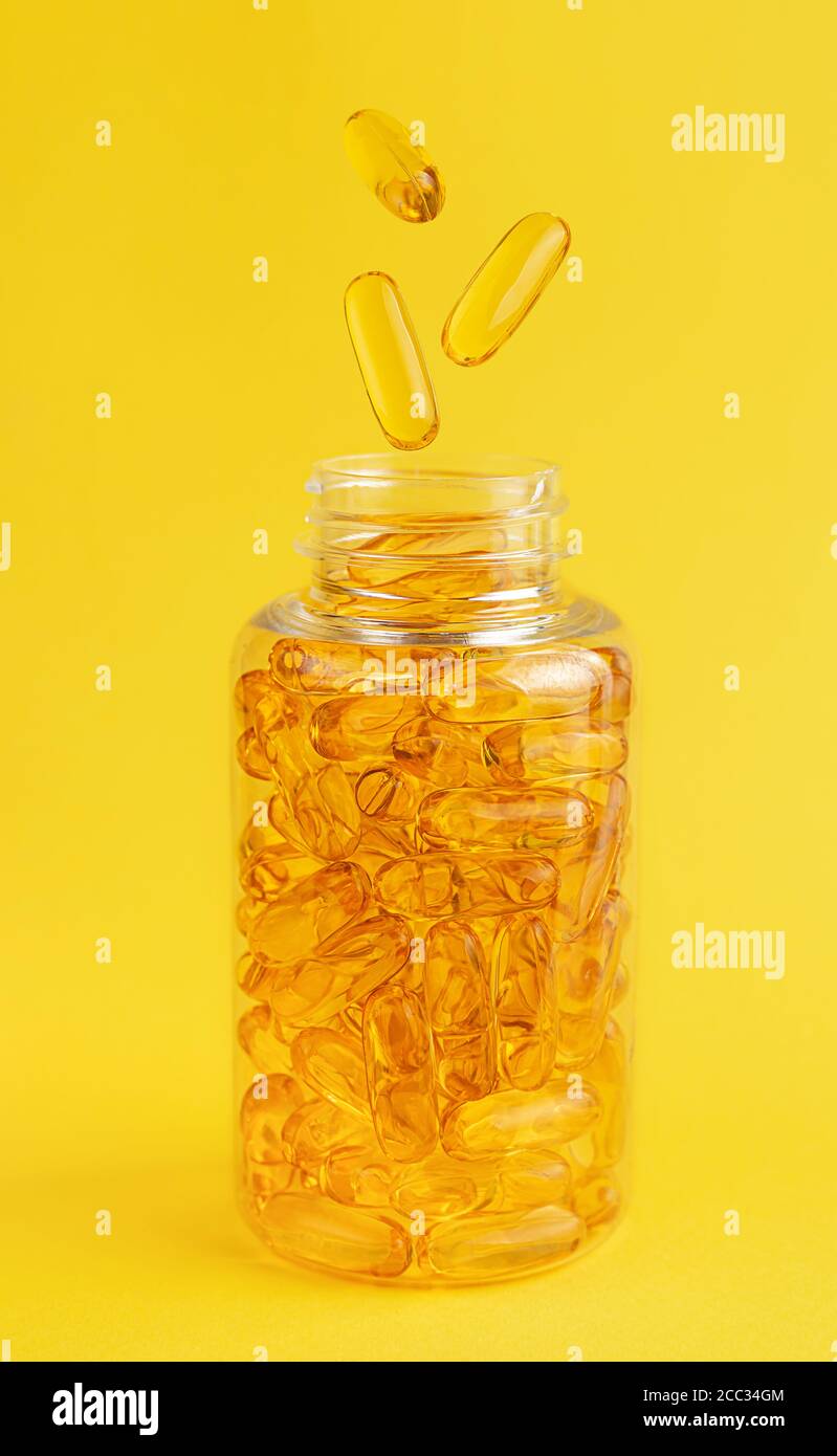 Fish oil capsules falling into the bottle on yellow background ...