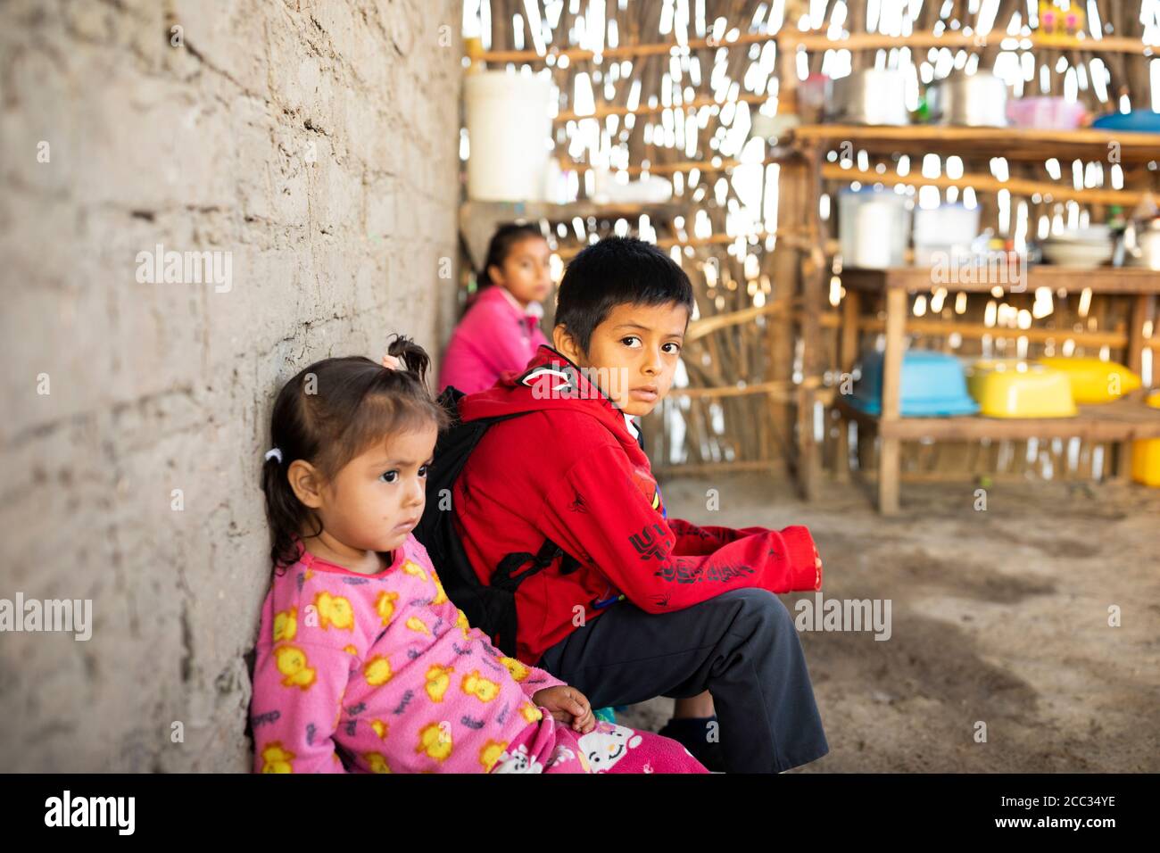 Three children sit inside their mud and stick constructed home in rural ...