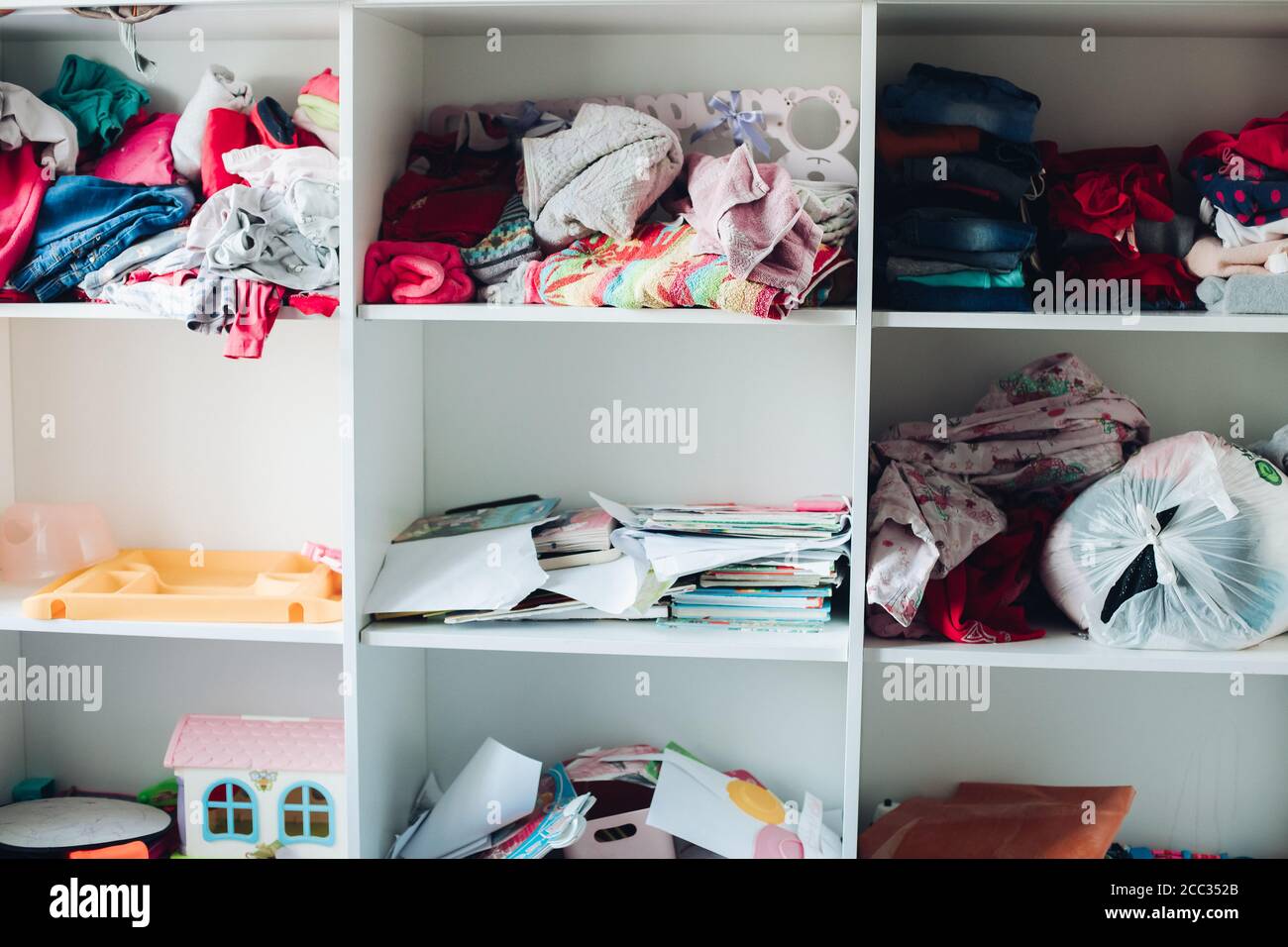 A large white cupboard with square shelves and things not folded on ...