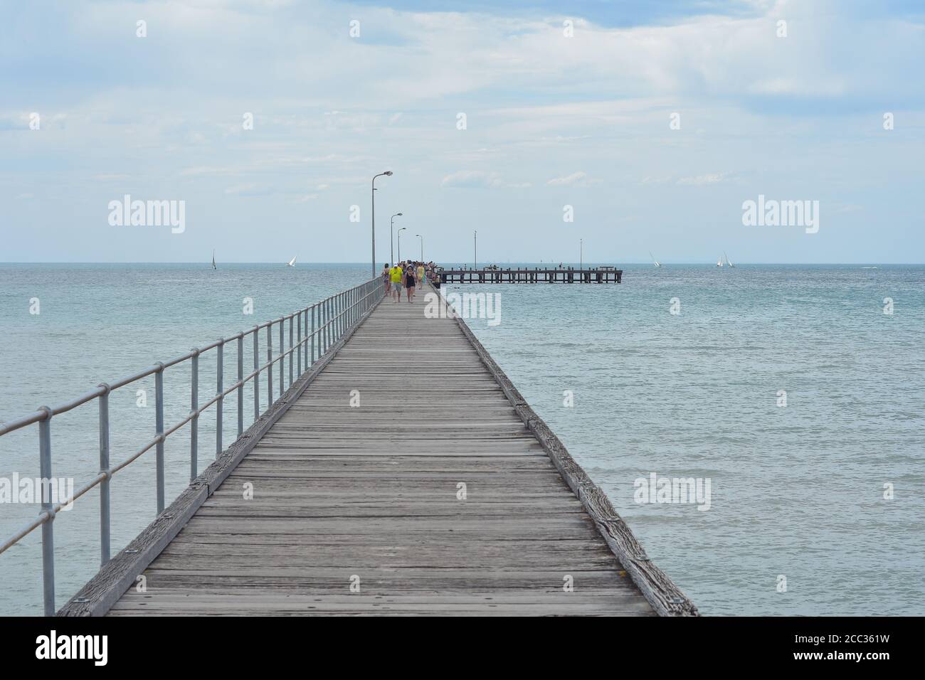People walking on long wooden wharf stretching over sandy shallows far ...
