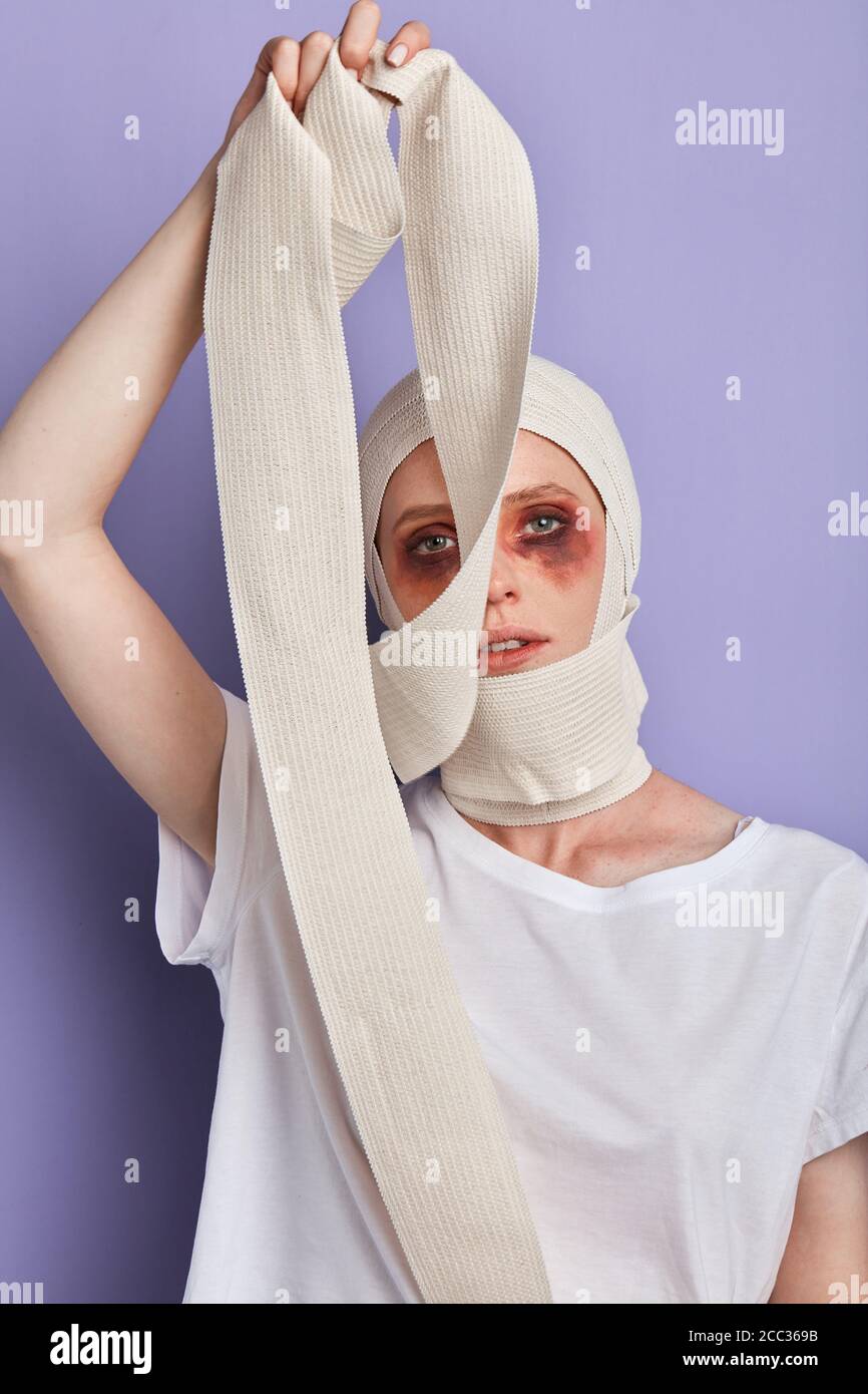 Young, unhappy and beautiful woman taking off bandage after surgery ...