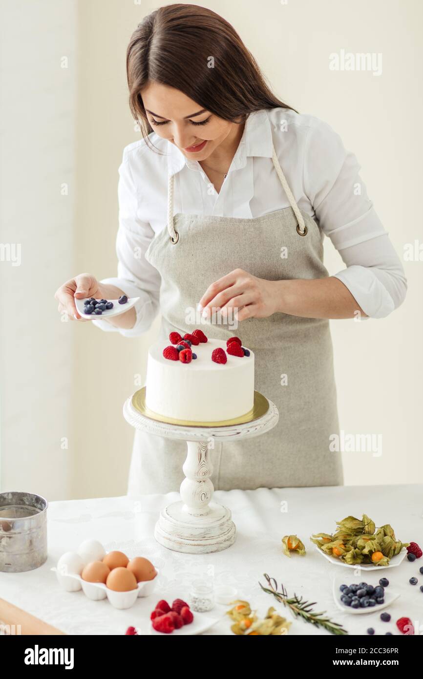 cheerful charming girl making up a decoration of cake at workplace ...