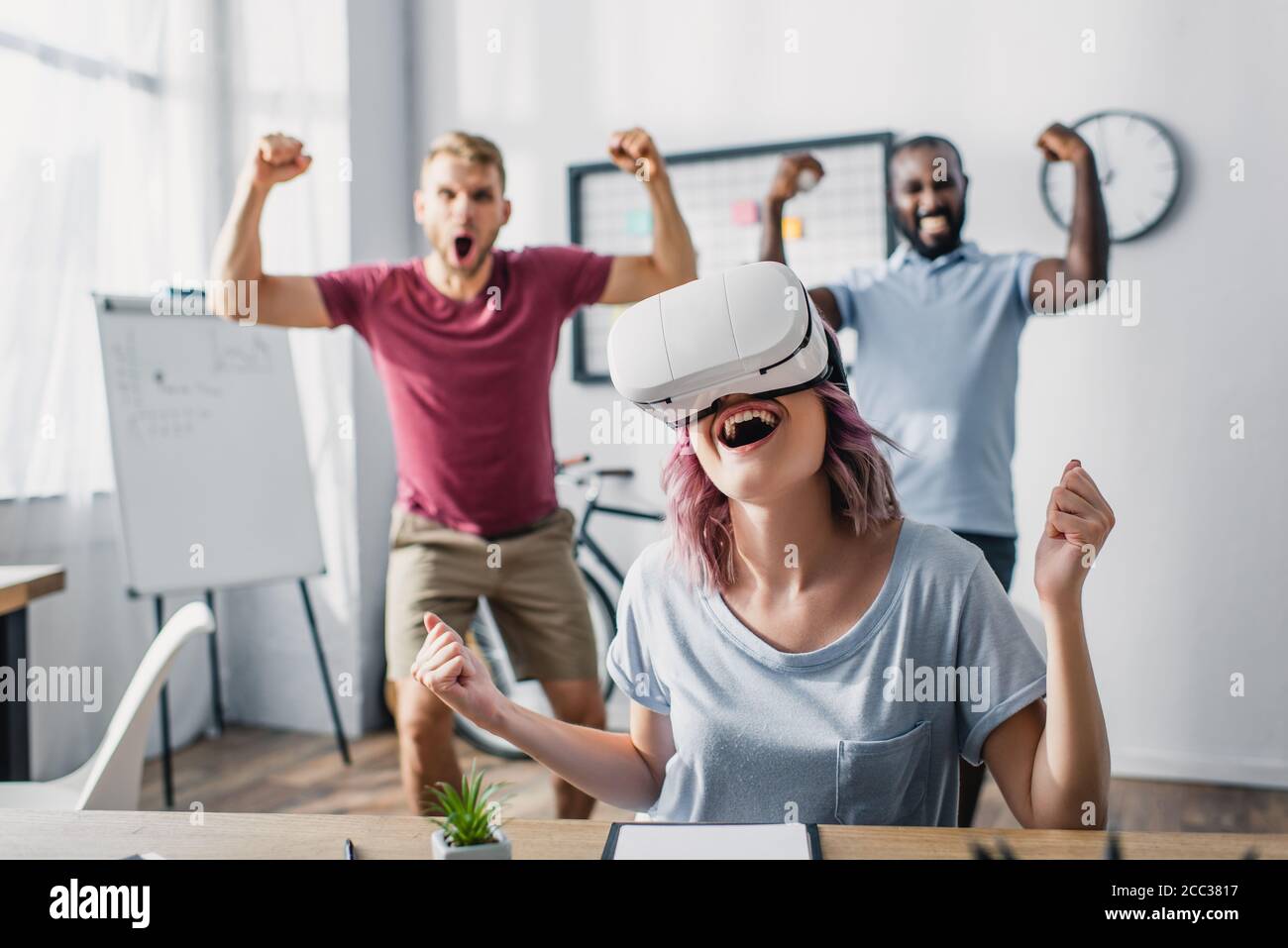 Selective focus of businesswoman in vr headset showing yes gesture with multicultural colleagues ...