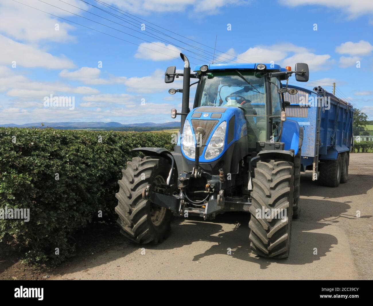 A large blue tractor with enormous tyres, parked by a hedge at ...