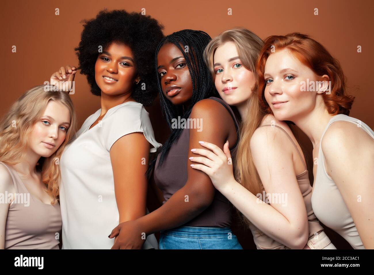 young pretty african and caucasian women posing cheerful together on brown background, lifestyle ...