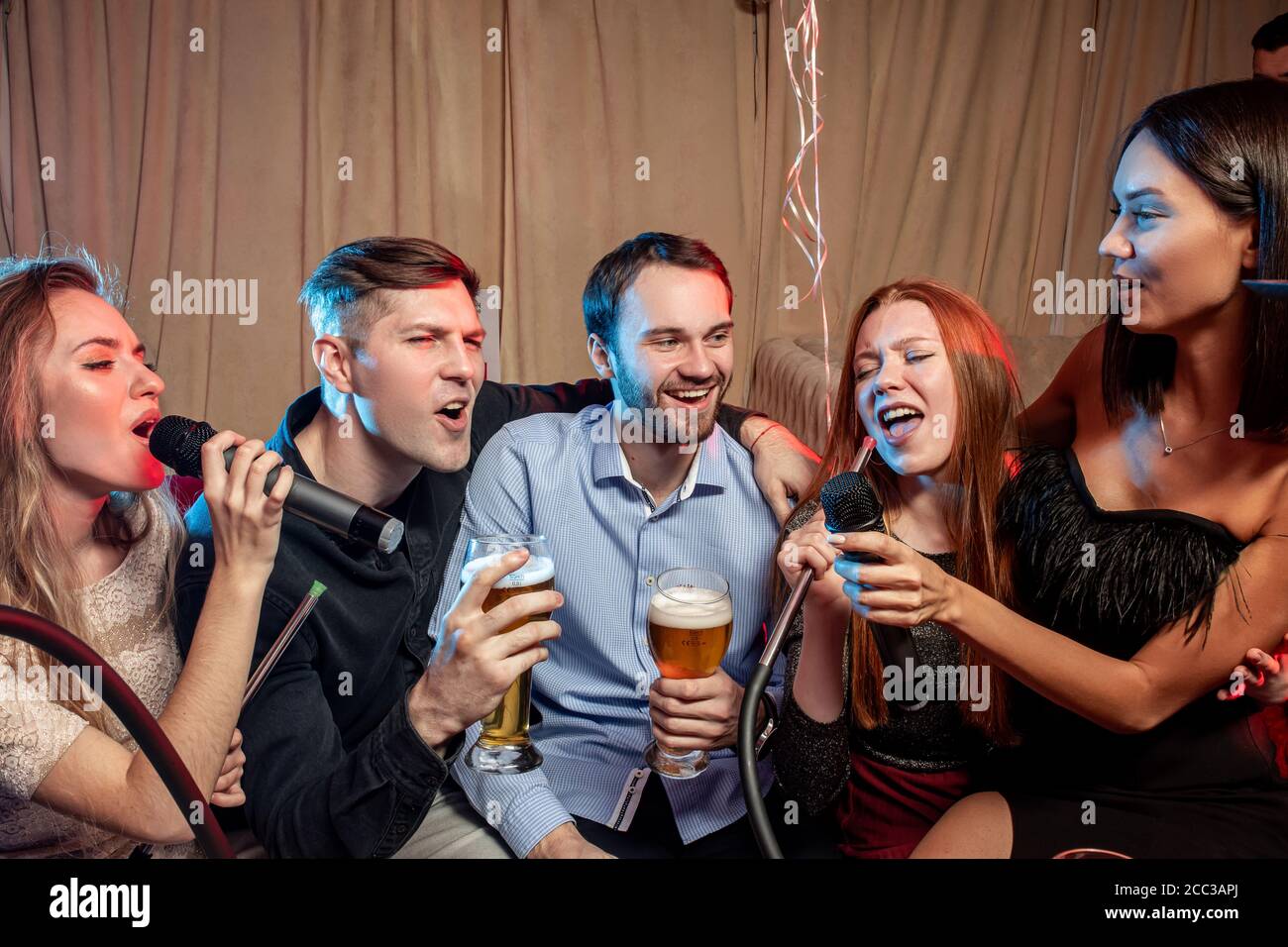 young people drinking beer, singing and smoking hookah in karaoke bar ...