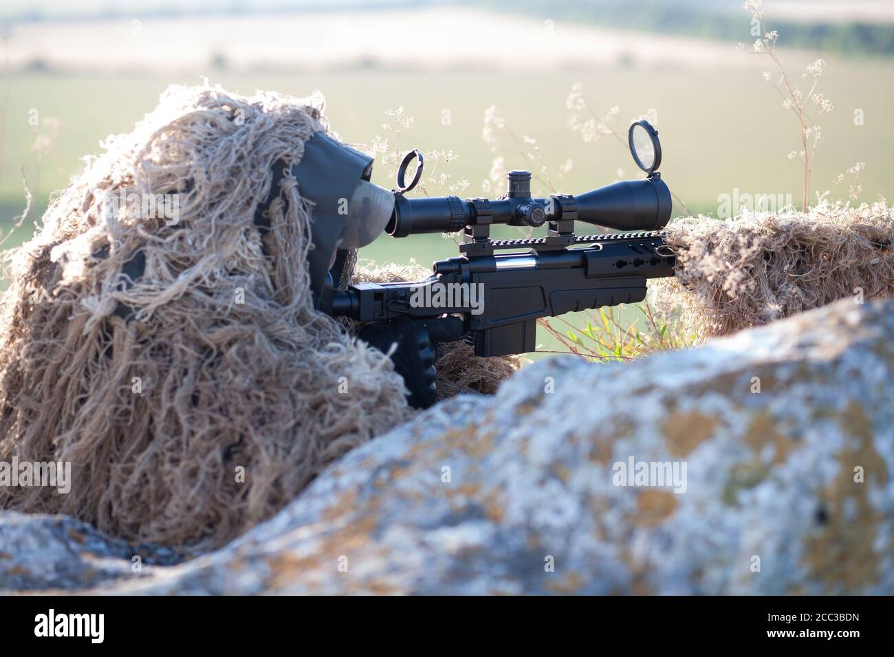 sniper in ghillie suit with precision rifle with optic sight on combat ...