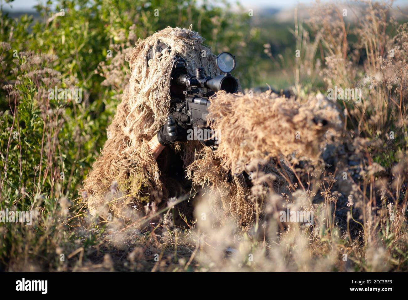 sniper in ghillie suit with precision rifle with optic sight on combat ...