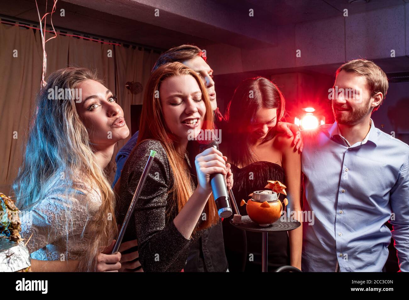 group of young people together in karaoke bar, singing and having fun ...