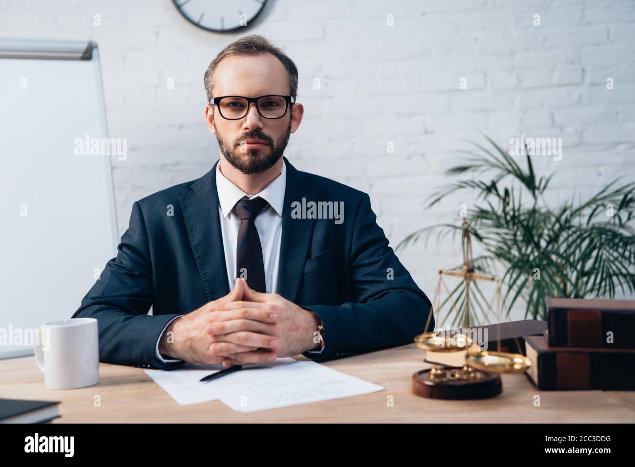 bearded lawyer in glasses looking at camera and sitting with clenched ...