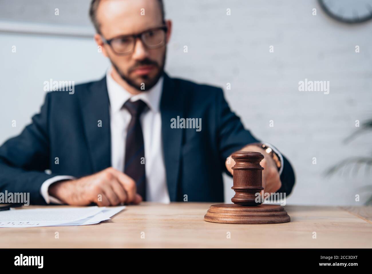 selective focus of bearded judge holding gavel near papers on table ...