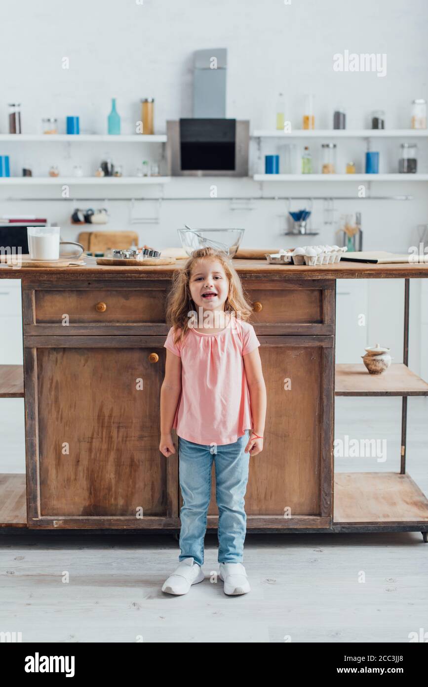 full lengtn view of girl standing near kitchen table with ingredients ...