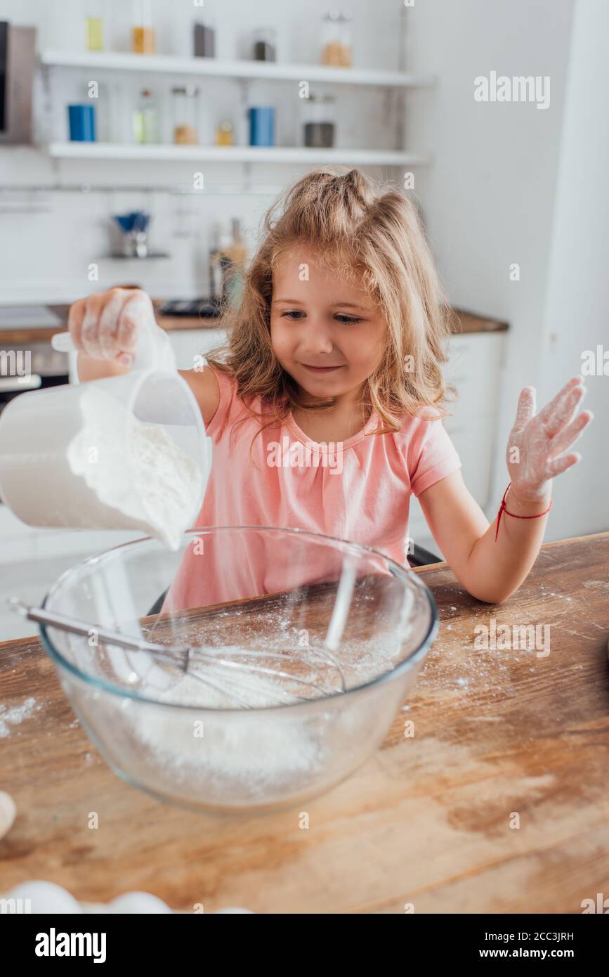 little girl pouring flour into glass bowl while cooking in kitchen ...