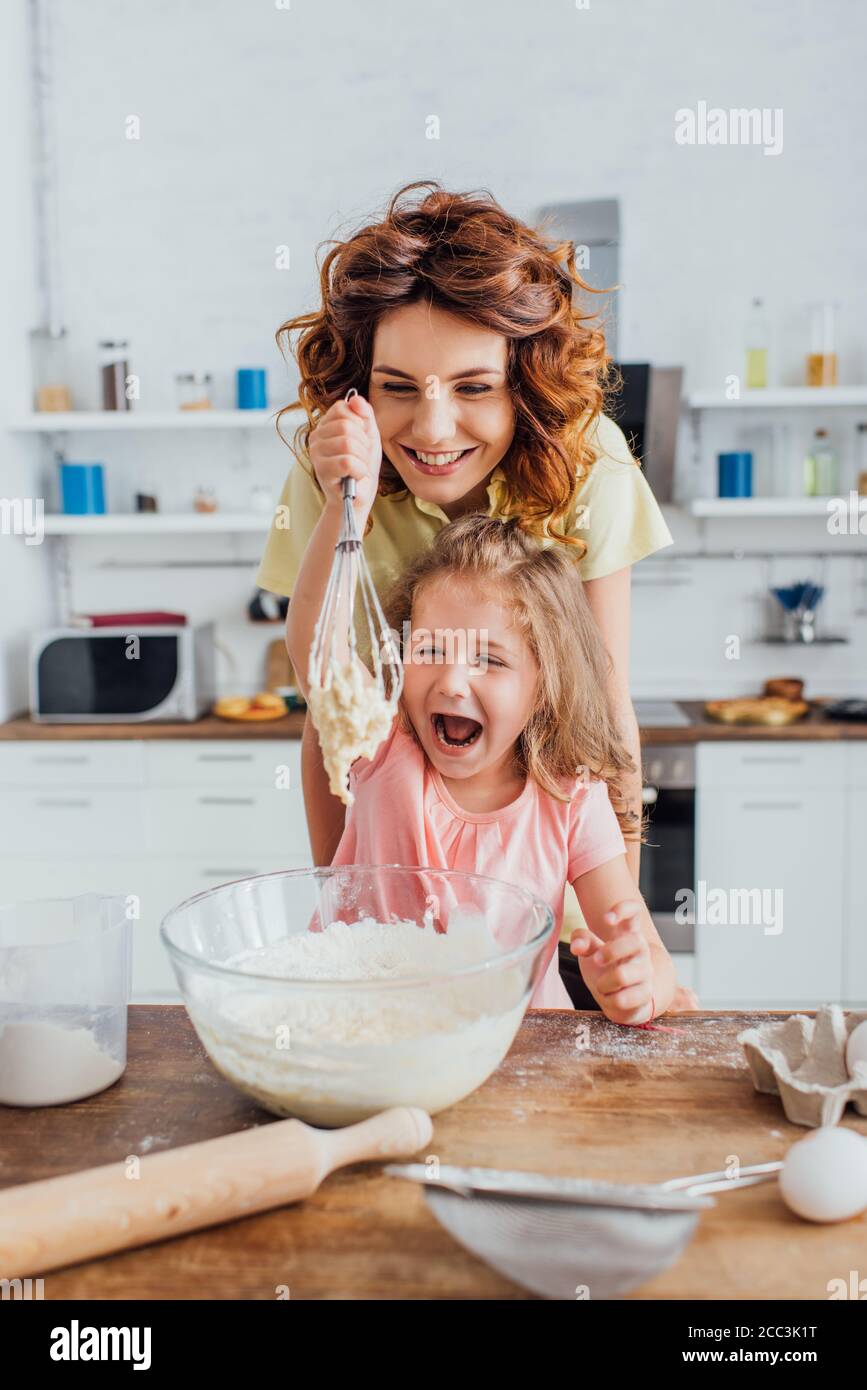 selective focus of excited girl holding whisk with dough near mother Stock Photo - Alamy