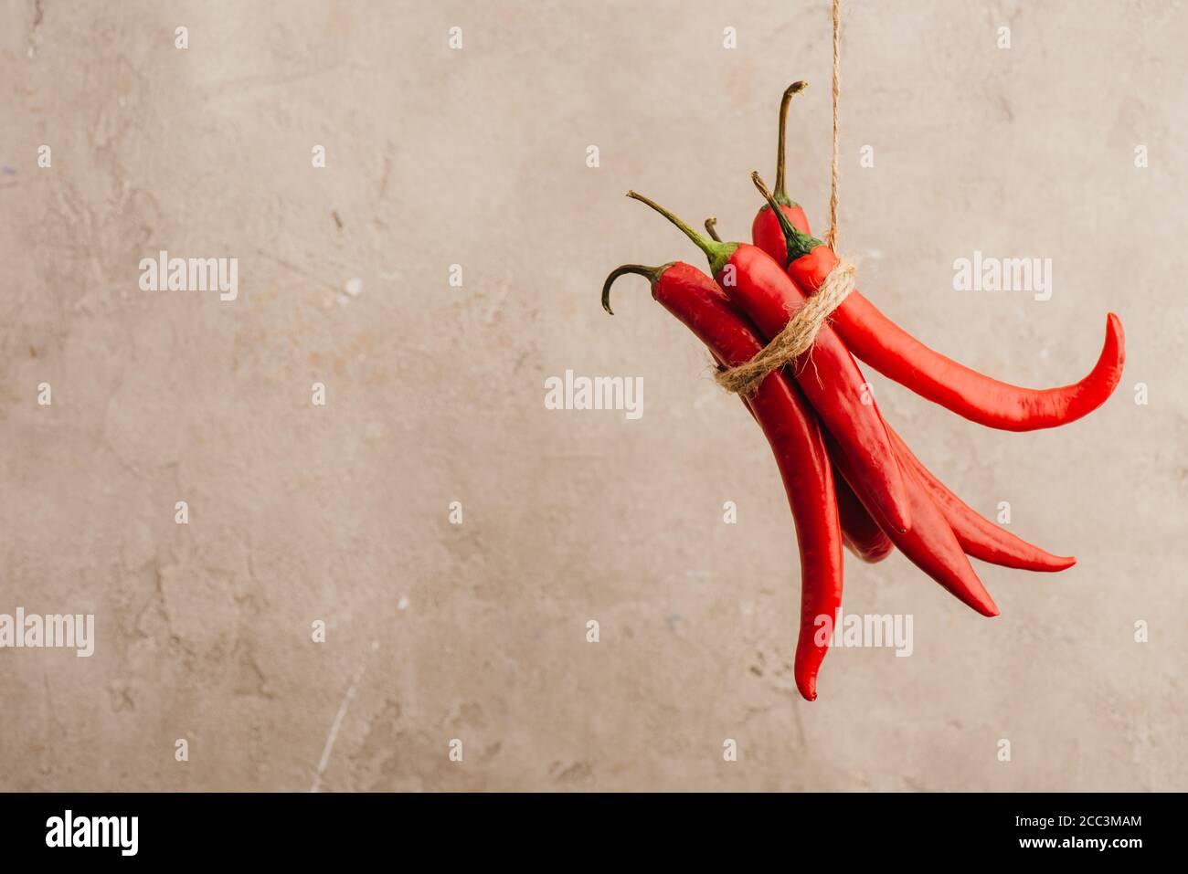 bunch of red chili peppers tied with rope hanging on beige concrete ...