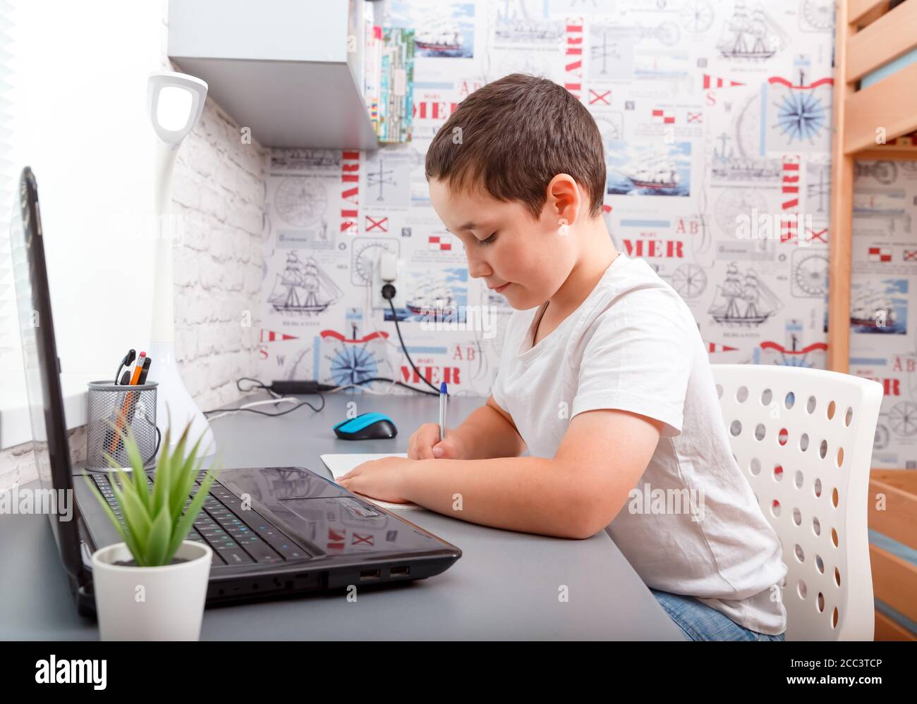 Happy caucasian schoolboy doing homework sitting at desk Homeschooling ...