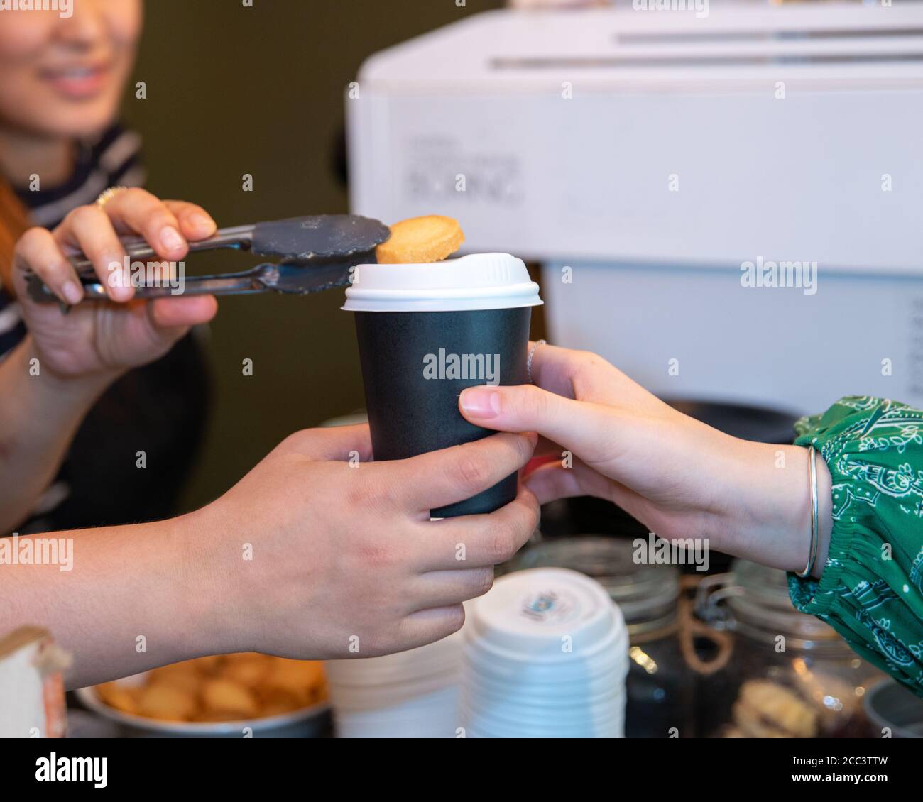 Barista giving a small cookie to a customer Stock Photo - Alamy
