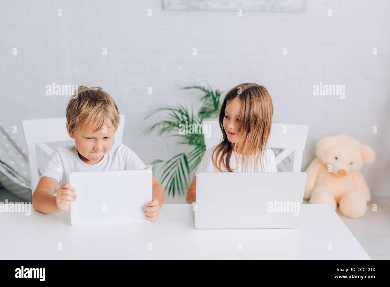brother and sister sitting at while table and using laptops together ...