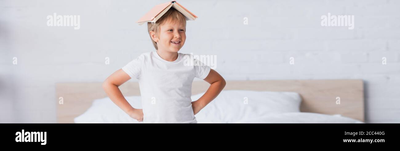excited boy in white t-shirt standing with book on head and hands on ...