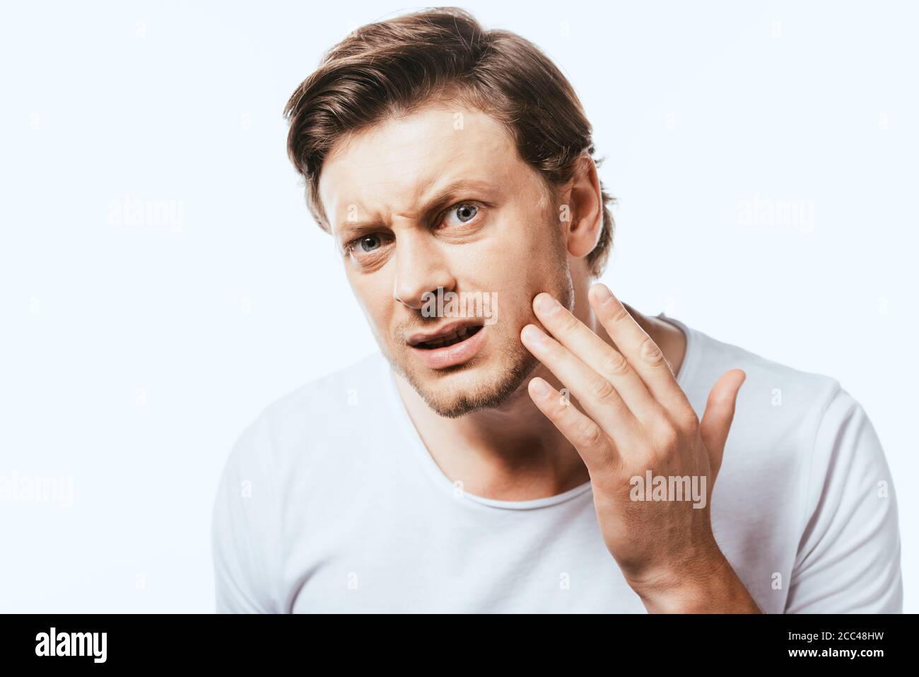 Worried man looking at camera and touching skin on cheek isolated on ...