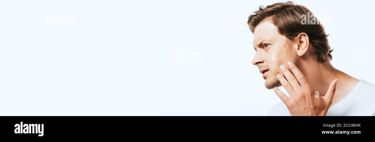 Horizontal crop of focused man touching skin on cheek isolated on white ...