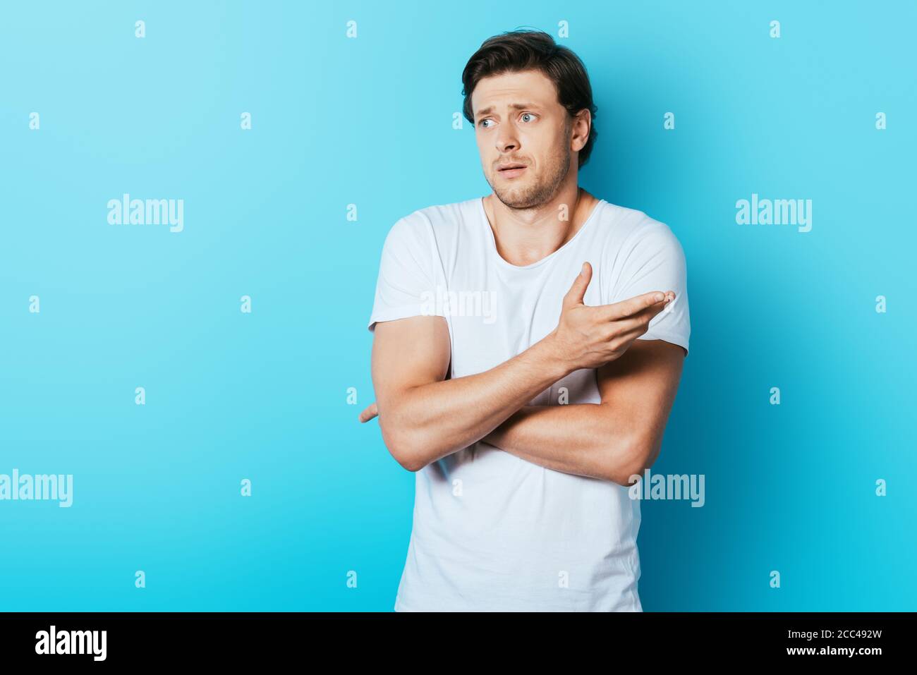 Confused man pointing with hand while looking away on blue background ...