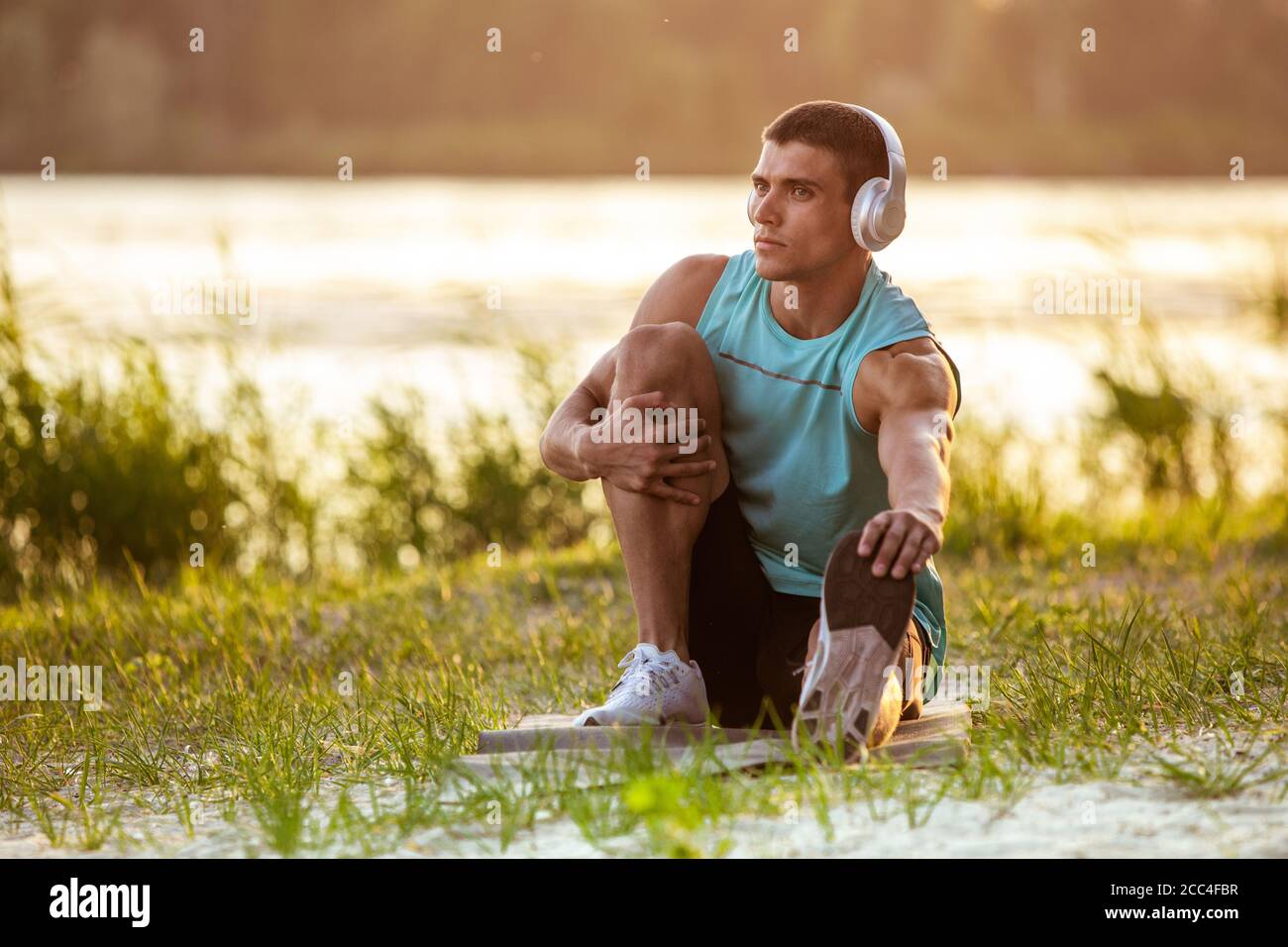 Stretching. A young athletic man working out, training listening to ...